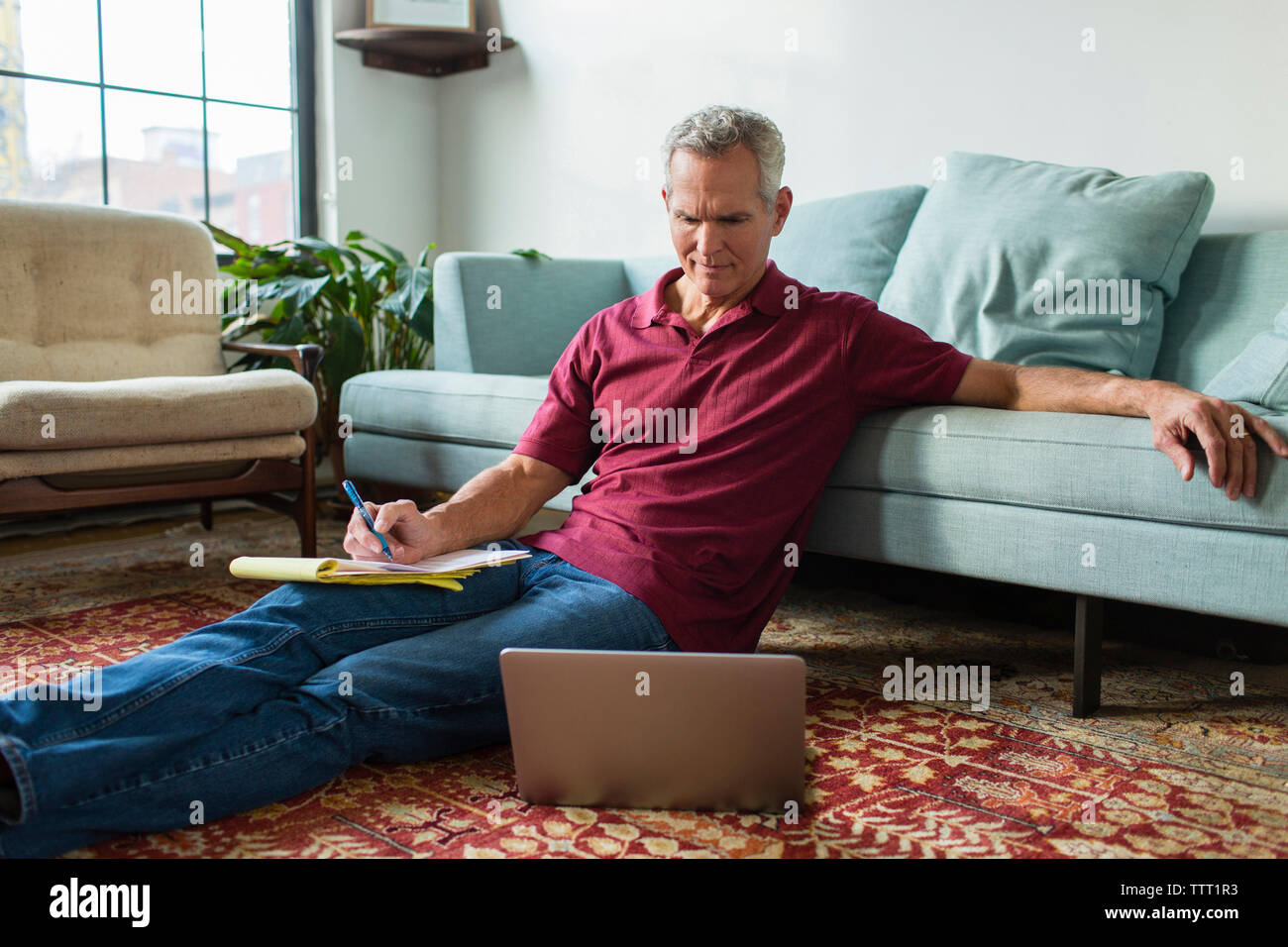 Serious mature man using laptop computer while sitting on carpet by ...
