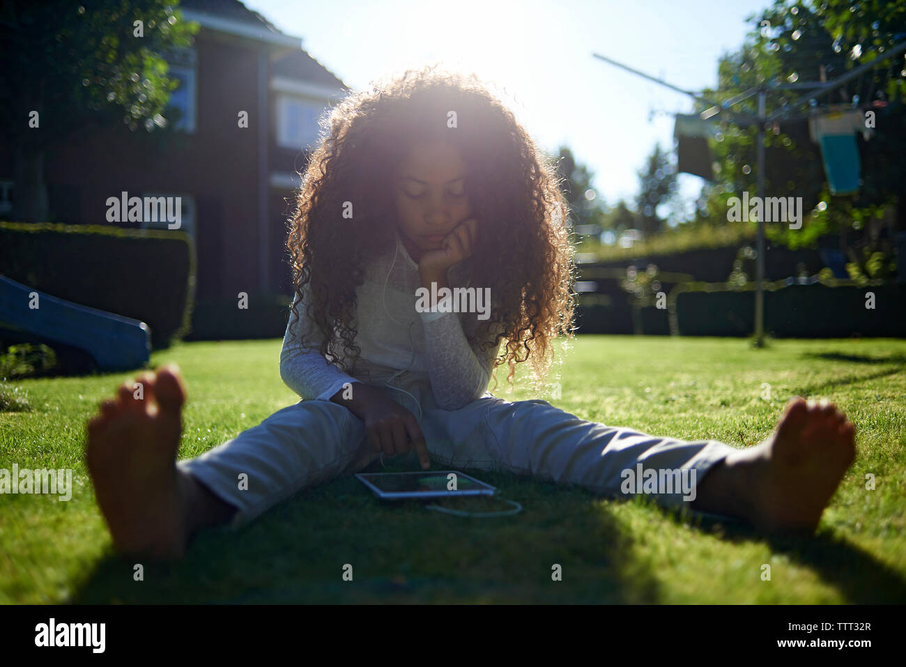Girl using tablet computer while sitting on grassy field in backyard ...