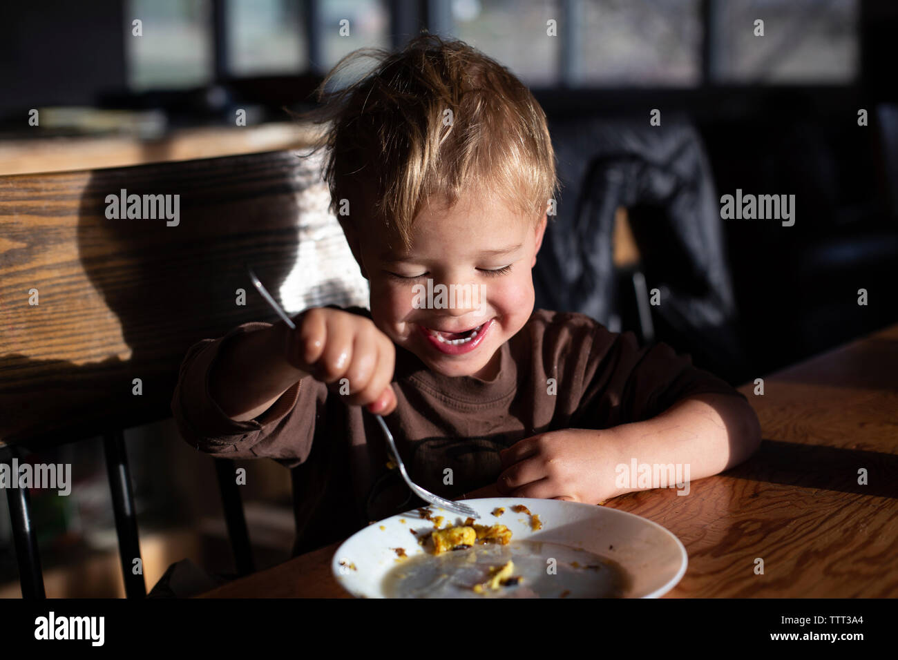 Close-up of cute happy boy eating food on wooden table while sitting at ...
