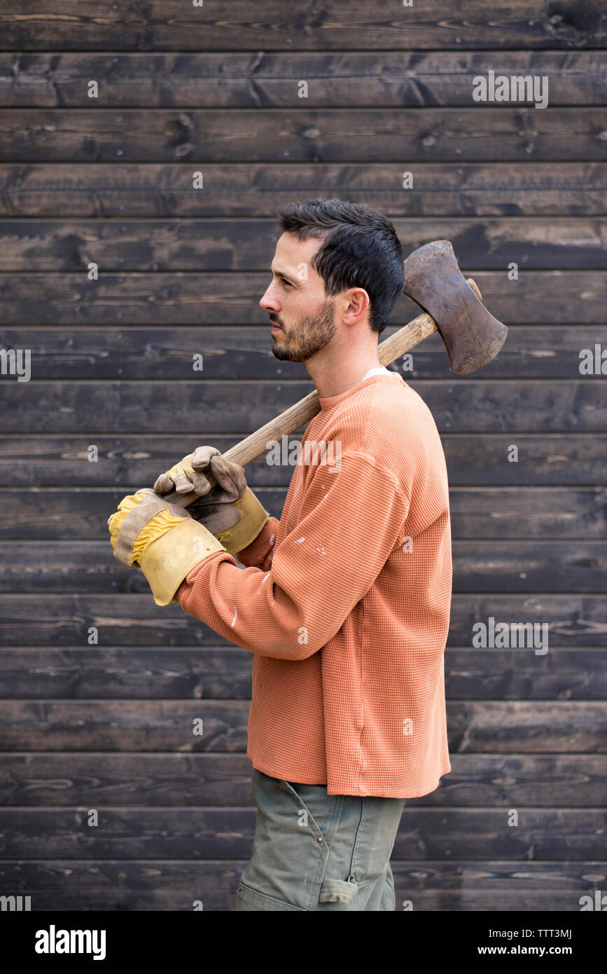 Side view of man holding axe while standing against cabin Stock Photo ...