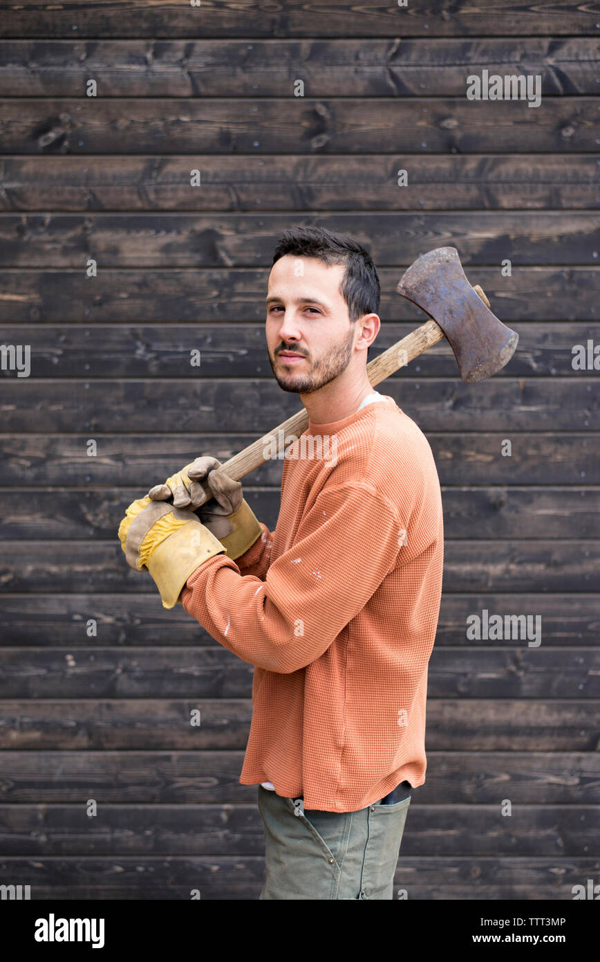 Portrait of man holding axe while standing against cabin Stock Photo ...