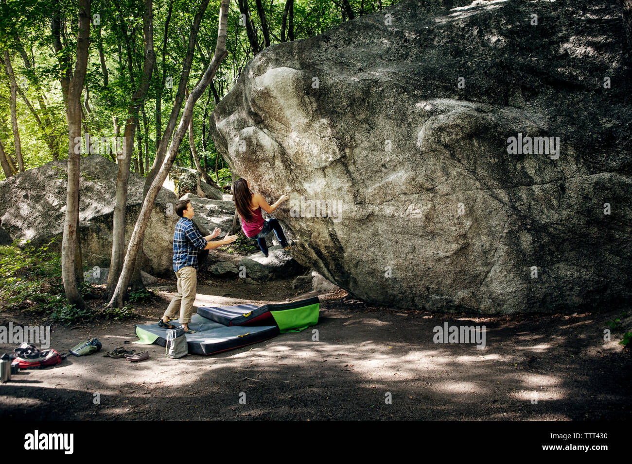 Man assisting woman in climbing rock at forest Stock Photo - Alamy