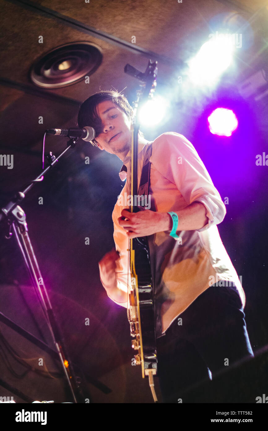 Low angle view of confident male singer singing and playing guitar in ...