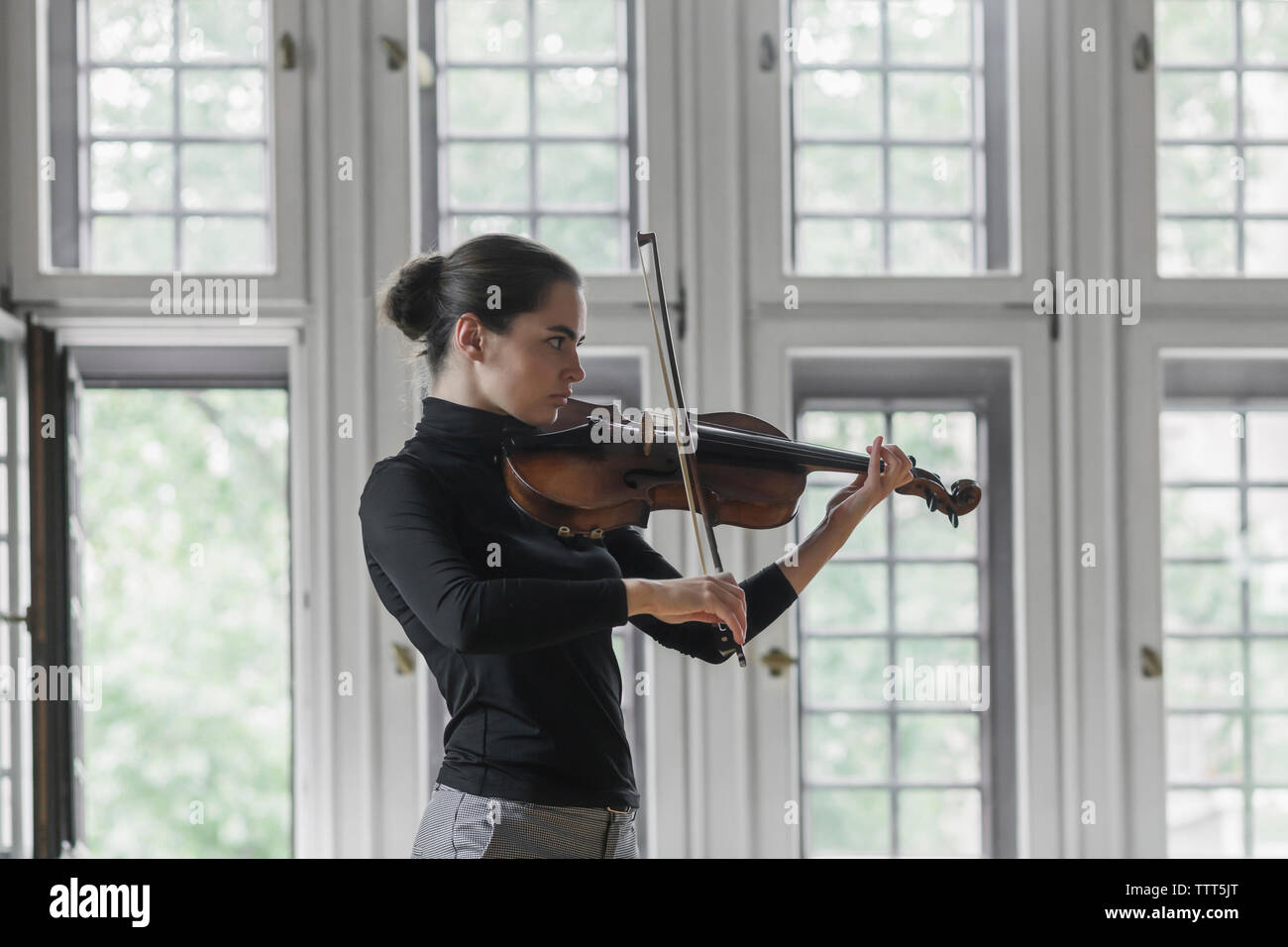 Side view of confident woman playing violin while standing against ...