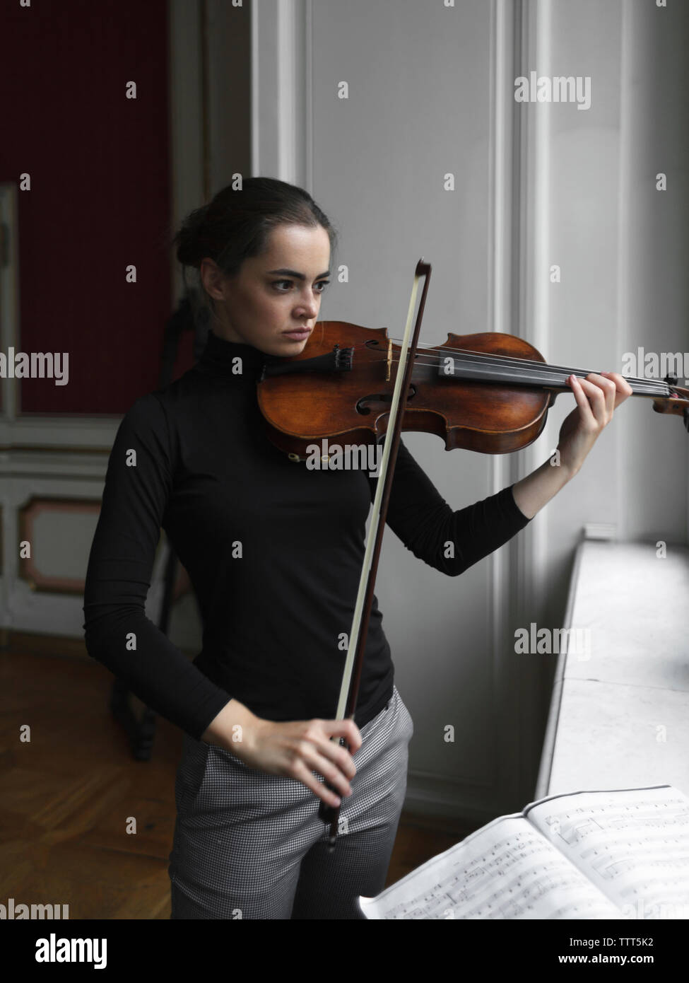 Confident woman with sheet music on window sill playing violin while ...