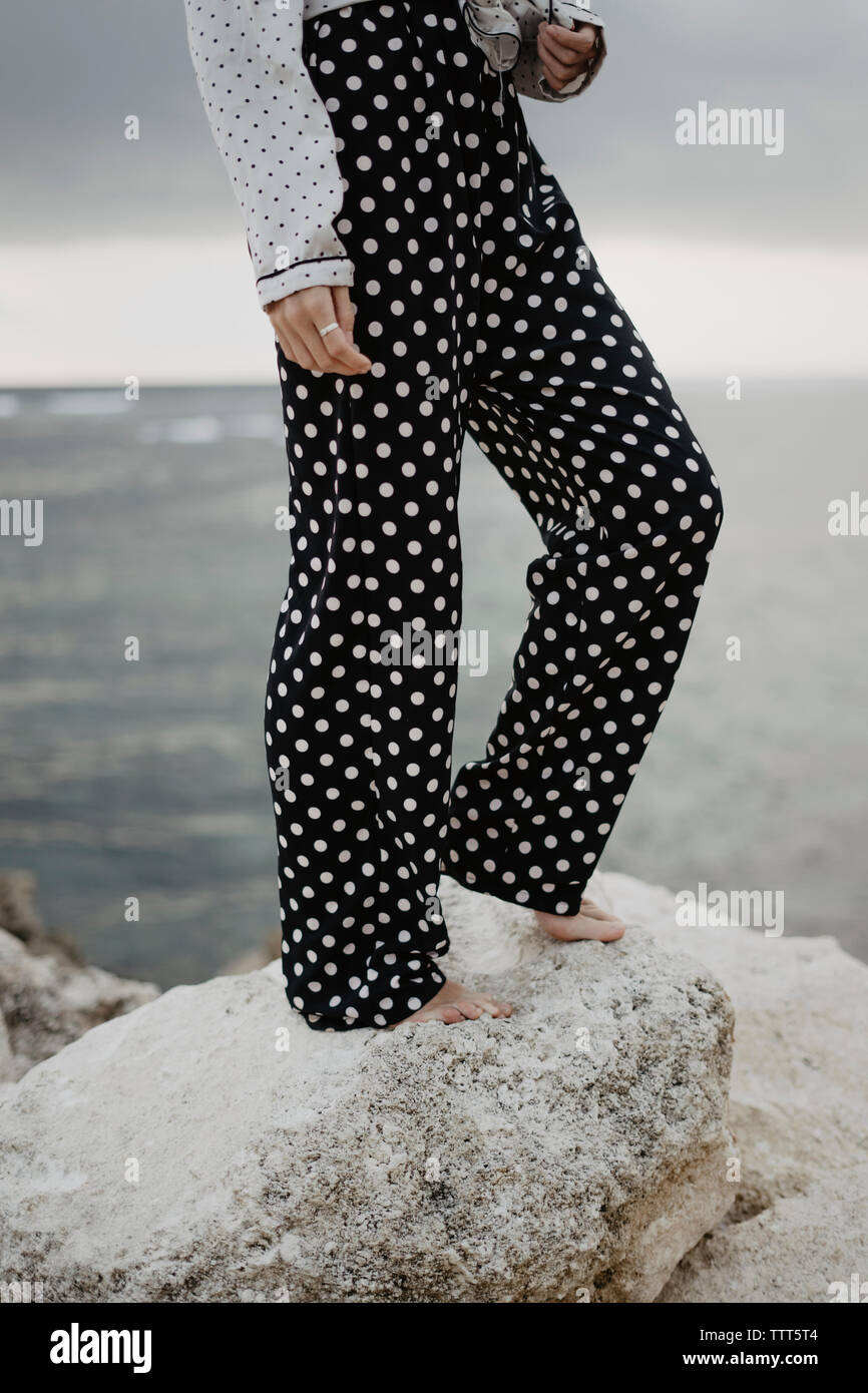 Low section of woman wearing spotted clothing while standing on rock at ...
