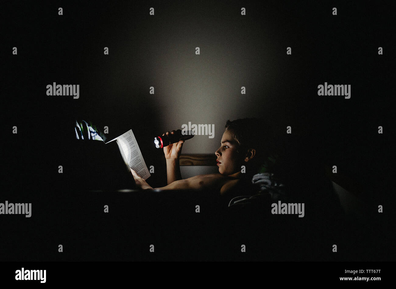 Boy holding flash light while reading book at home Stock Photo - Alamy