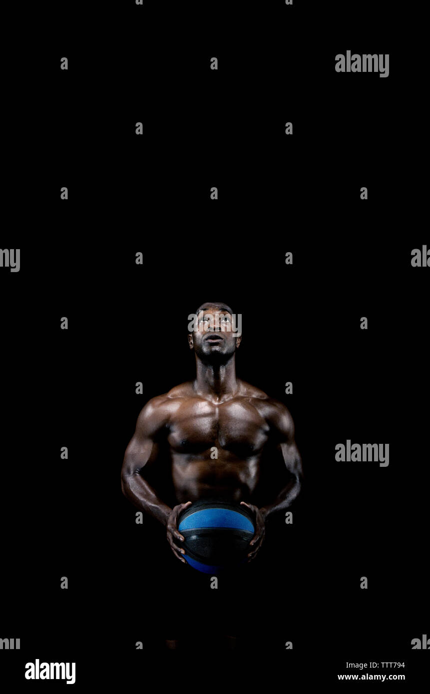 Muscular man holding ball while standing against black background Stock ...
