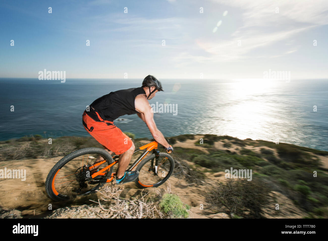 Side view of athlete riding bicycle on rock by sea Stock Photo - Alamy