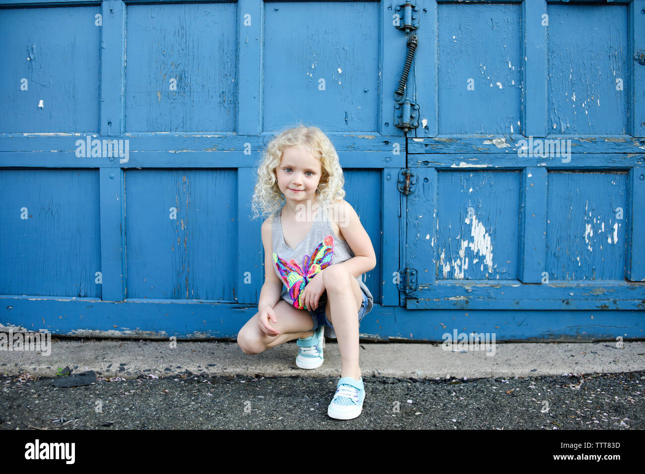 Portrait of girl crouching by blue door Stock Photo - Alamy
