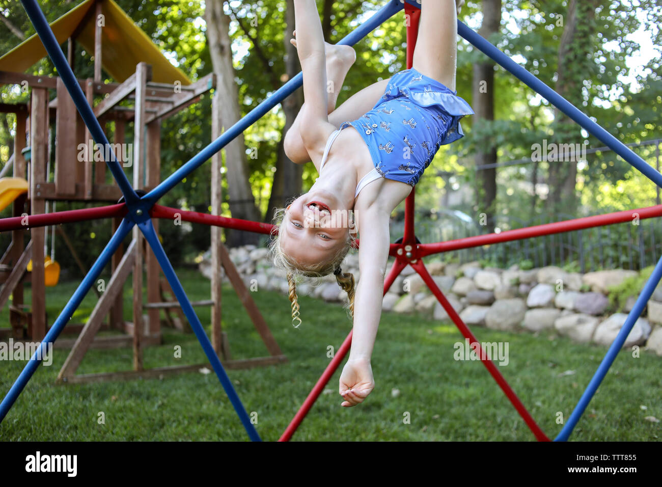 Portrait of cute happy girl hanging upside down on jungle gym against trees at playground Stock ...