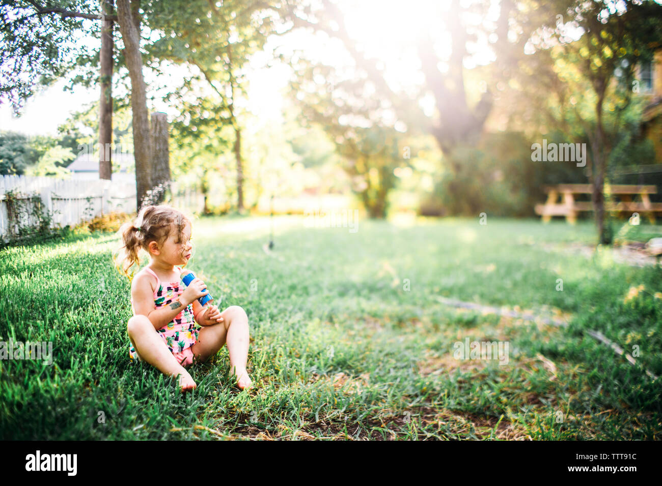 Full length of girl with popsicle sitting on grassy field at backyard ...