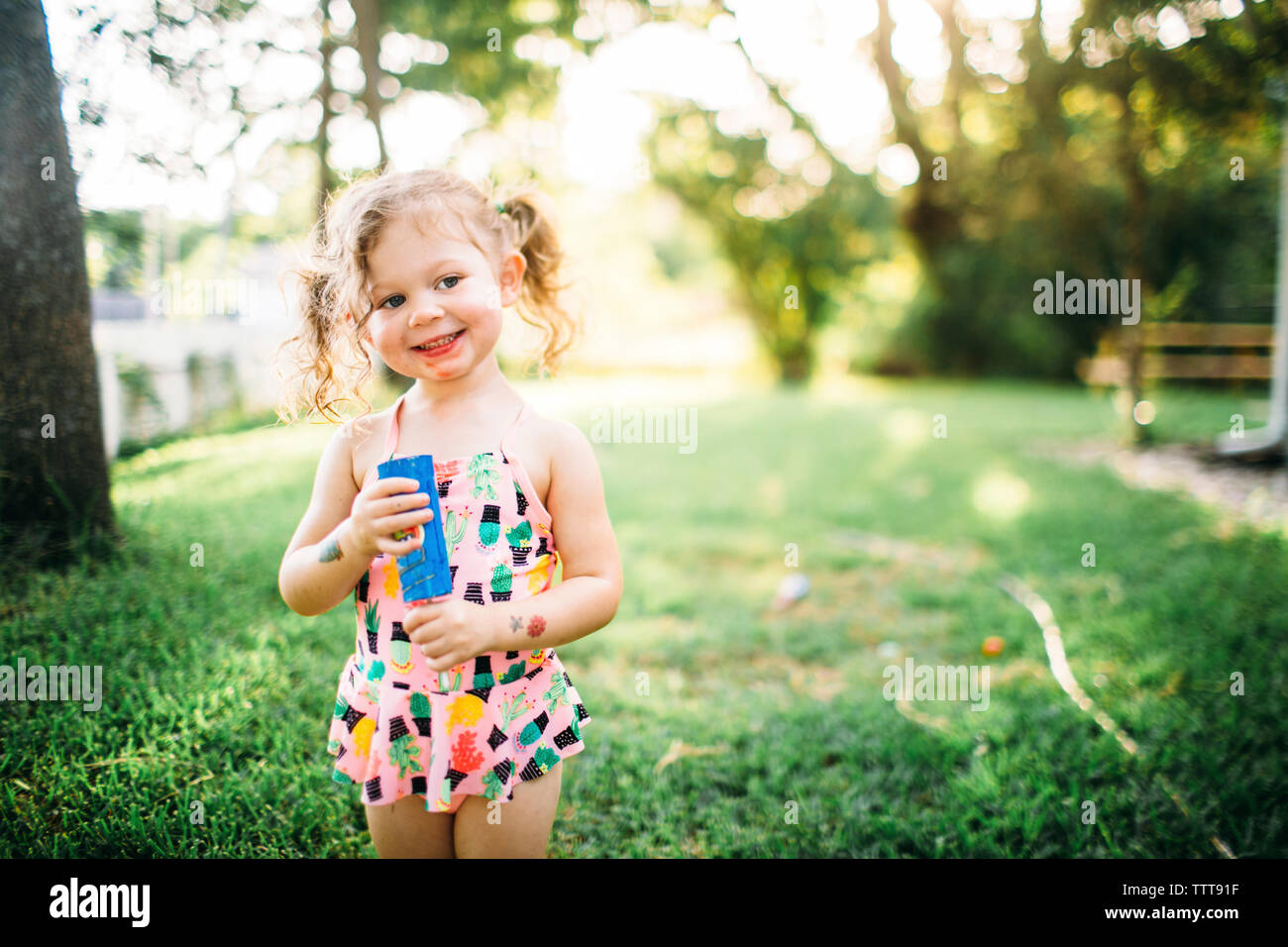 Smiling girl with popsicle standing on grassy field at backyard Stock ...