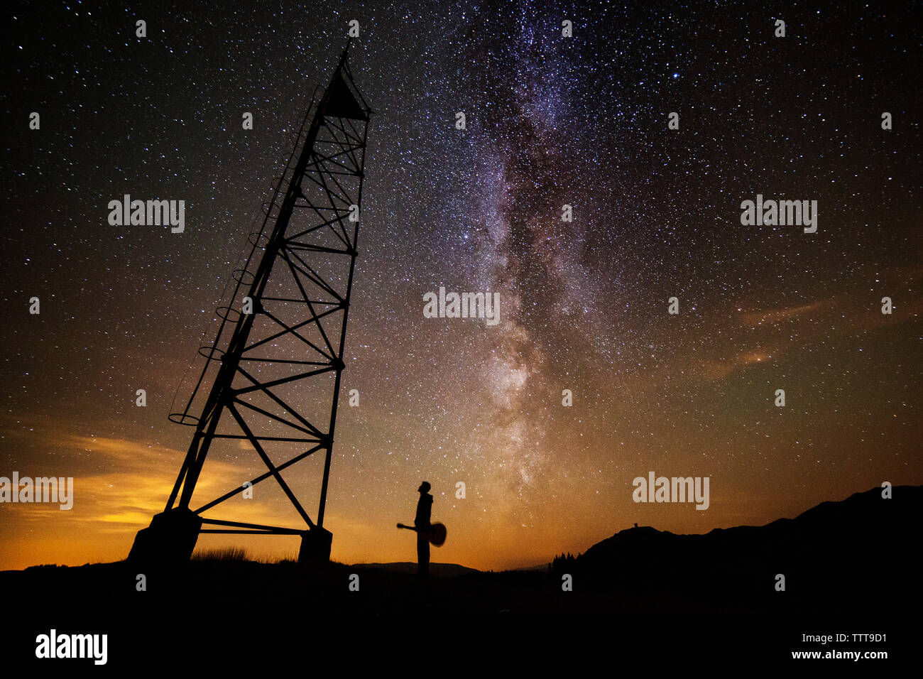 Silhouette man standing by lookout tower against starry sky at night ...