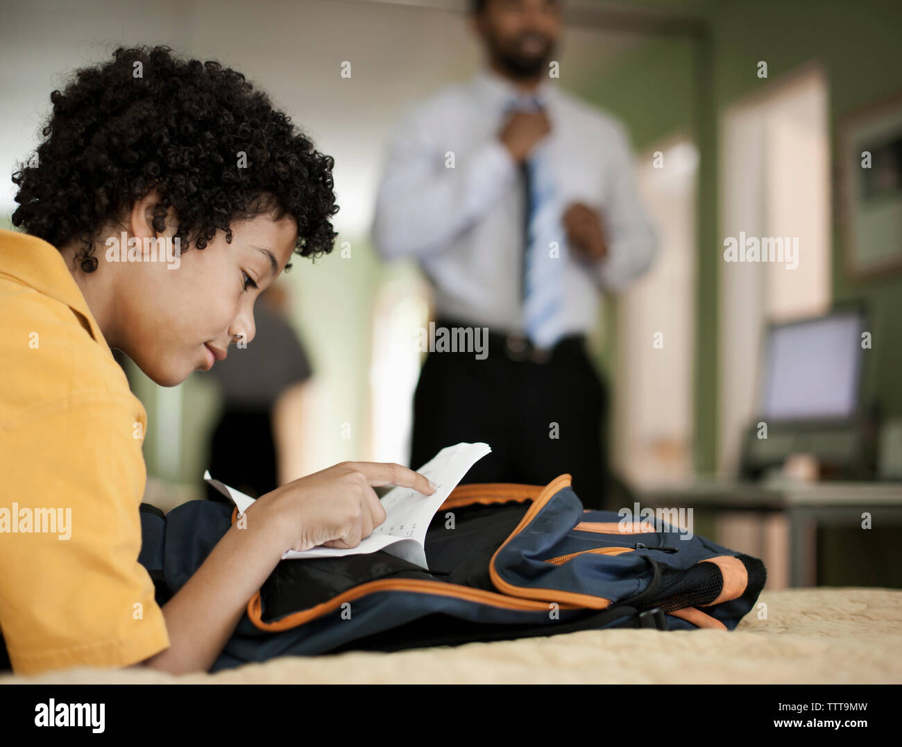Boy checking paper while father getting dressed in background Stock ...