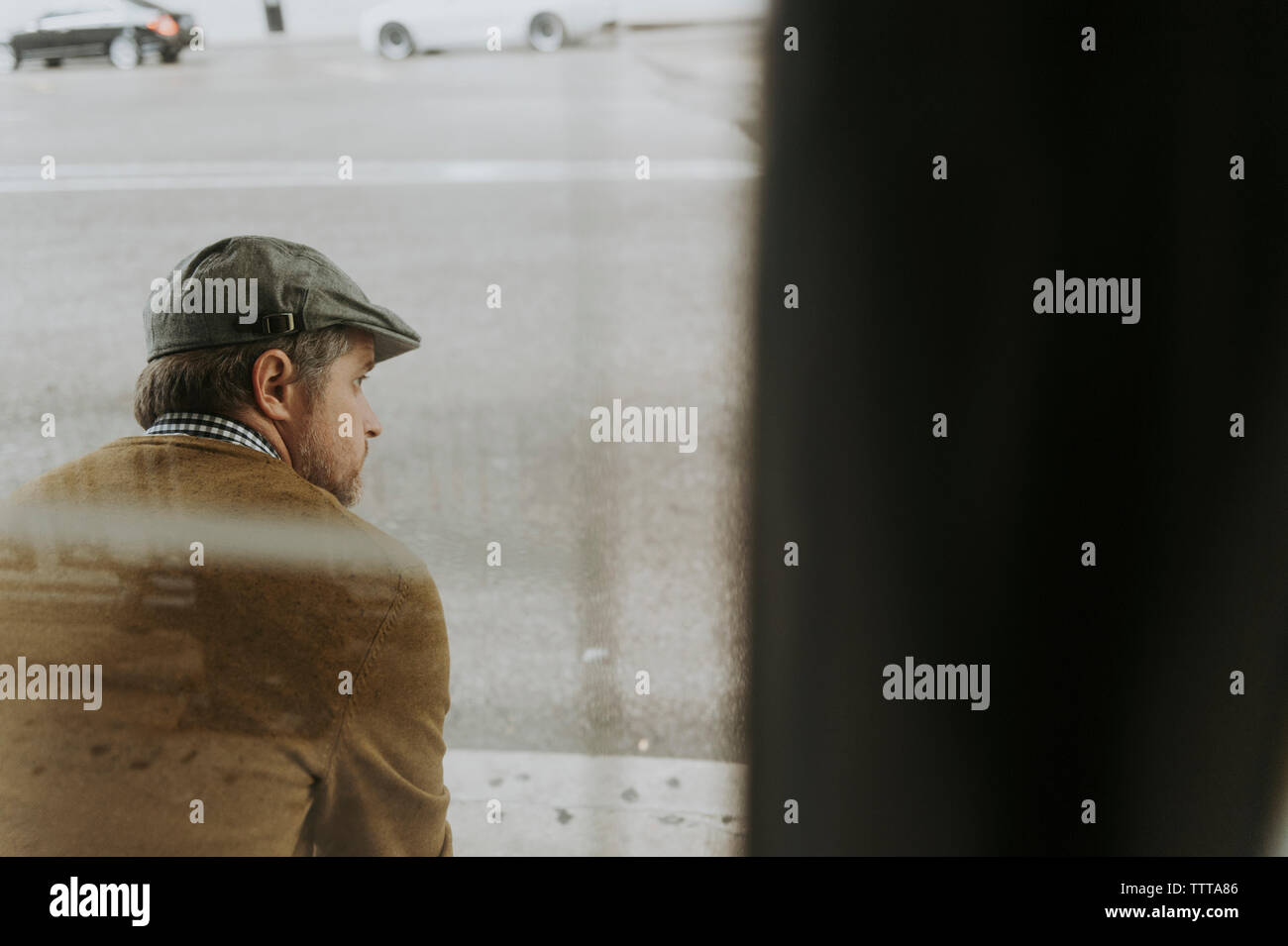 Rear view of thoughtful man looking away while sitting on street seen ...