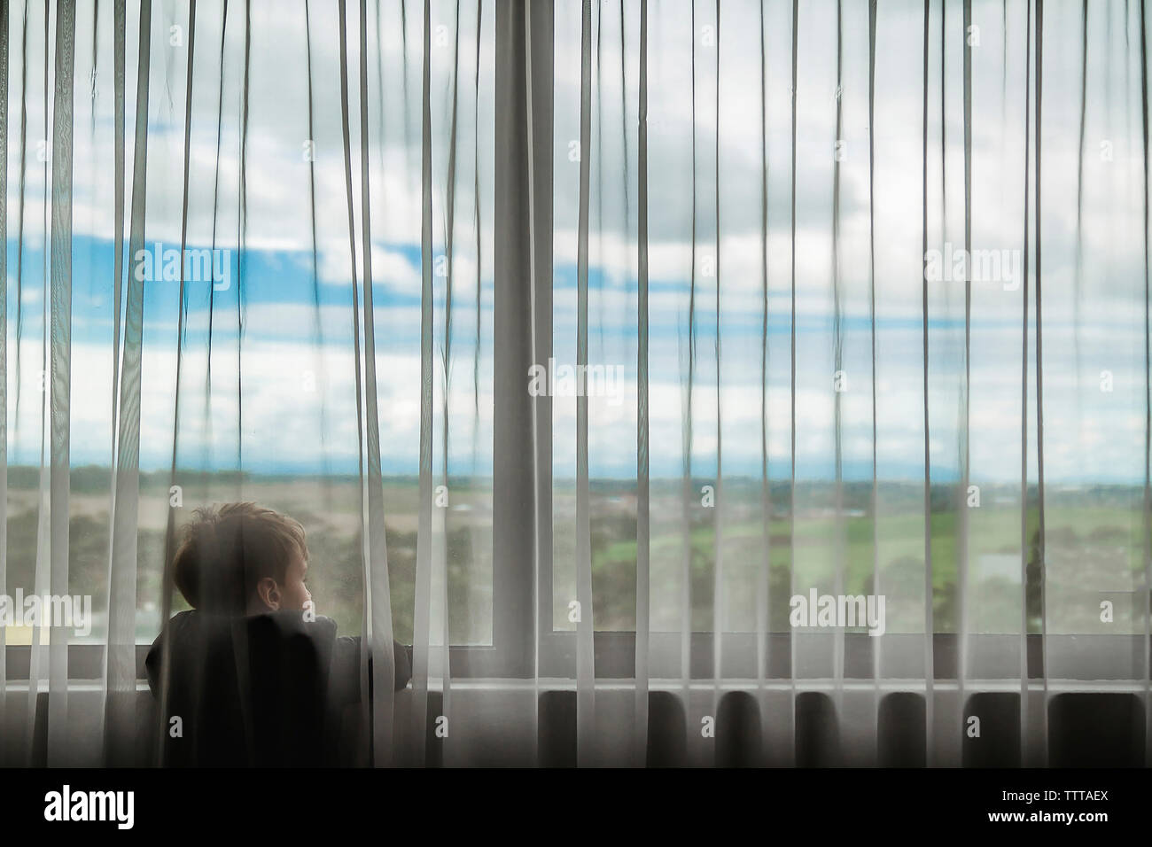 Rear view of boy looking through window while standing at home Stock ...
