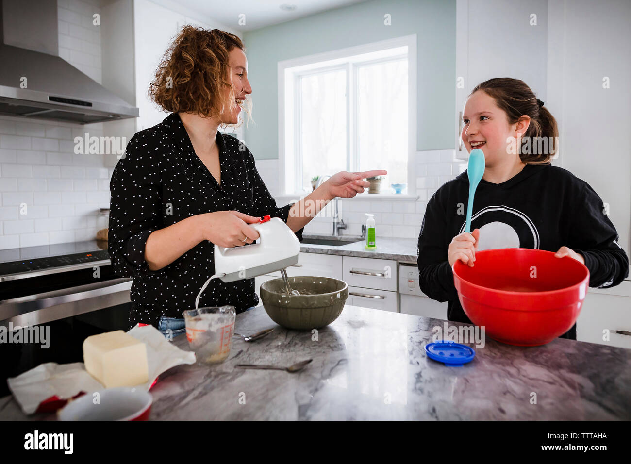 Mother guiding daughter in preparing food on kitchen island at home ...