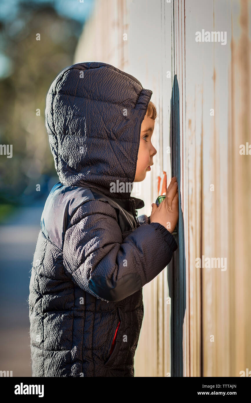 Side view of curious boy wearing hooded jacket while peeking through ...