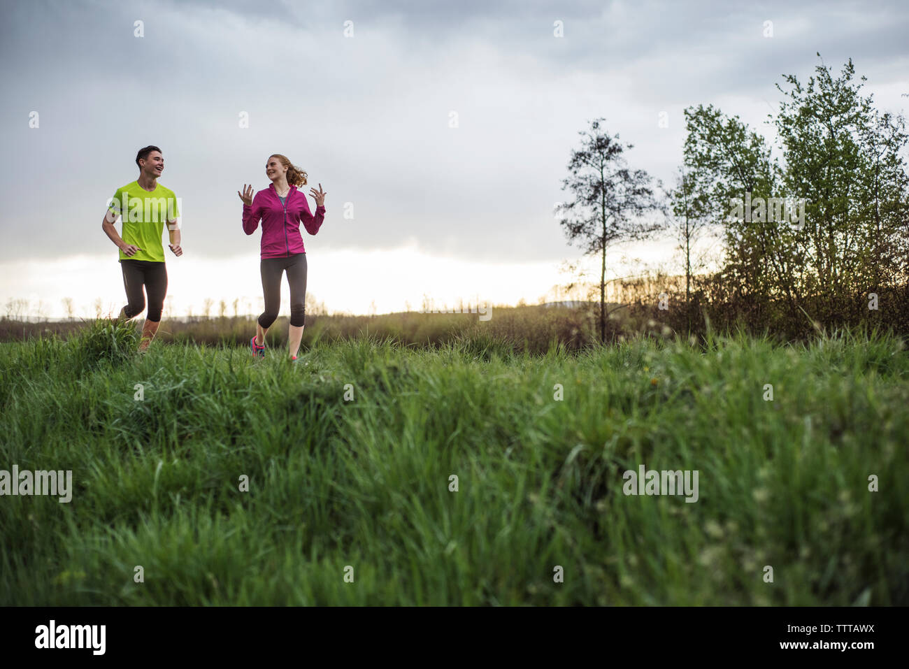 Happy friends talking while jogging on grassy field Stock Photo - Alamy