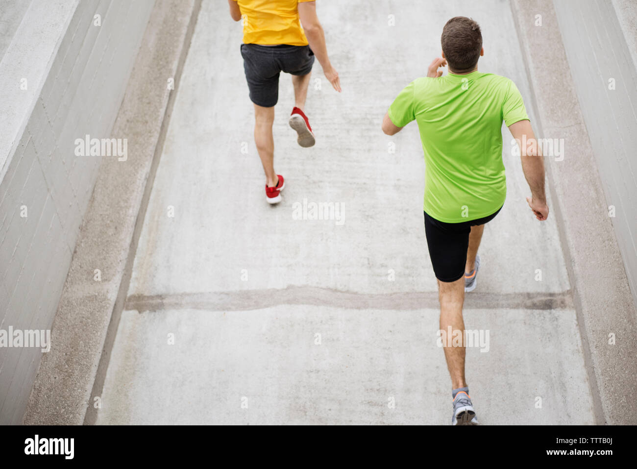 Rear view of male athletes running on footpath at parking lot Stock ...