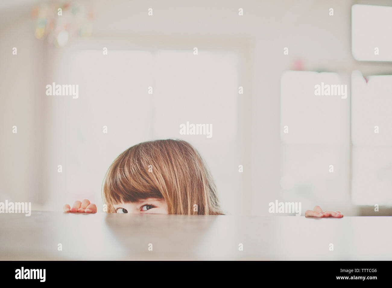 Portrait of girl peeking over table at home Stock Photo - Alamy