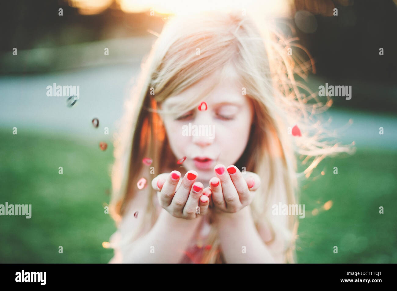 Cute girl blowing heart shapes at park Stock Photo - Alamy