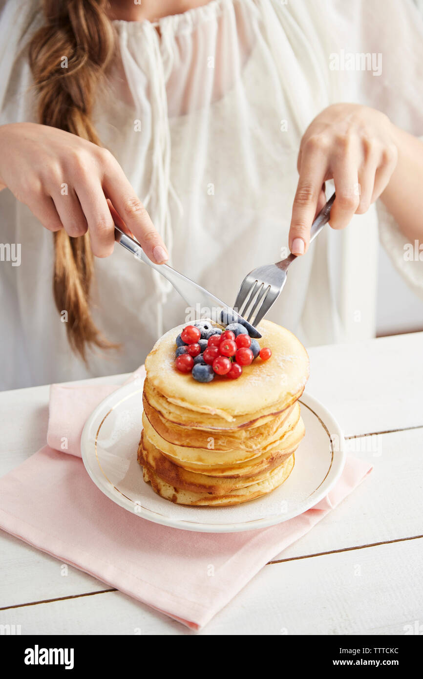 Midsection of woman eating pancakes on table while sitting at home ...