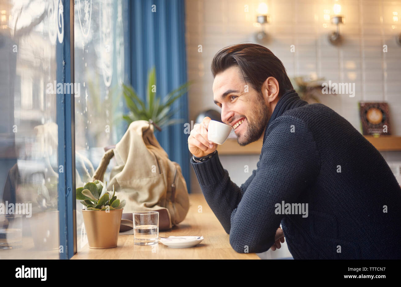 Side view of smiling man looking through window while having coffee by ...