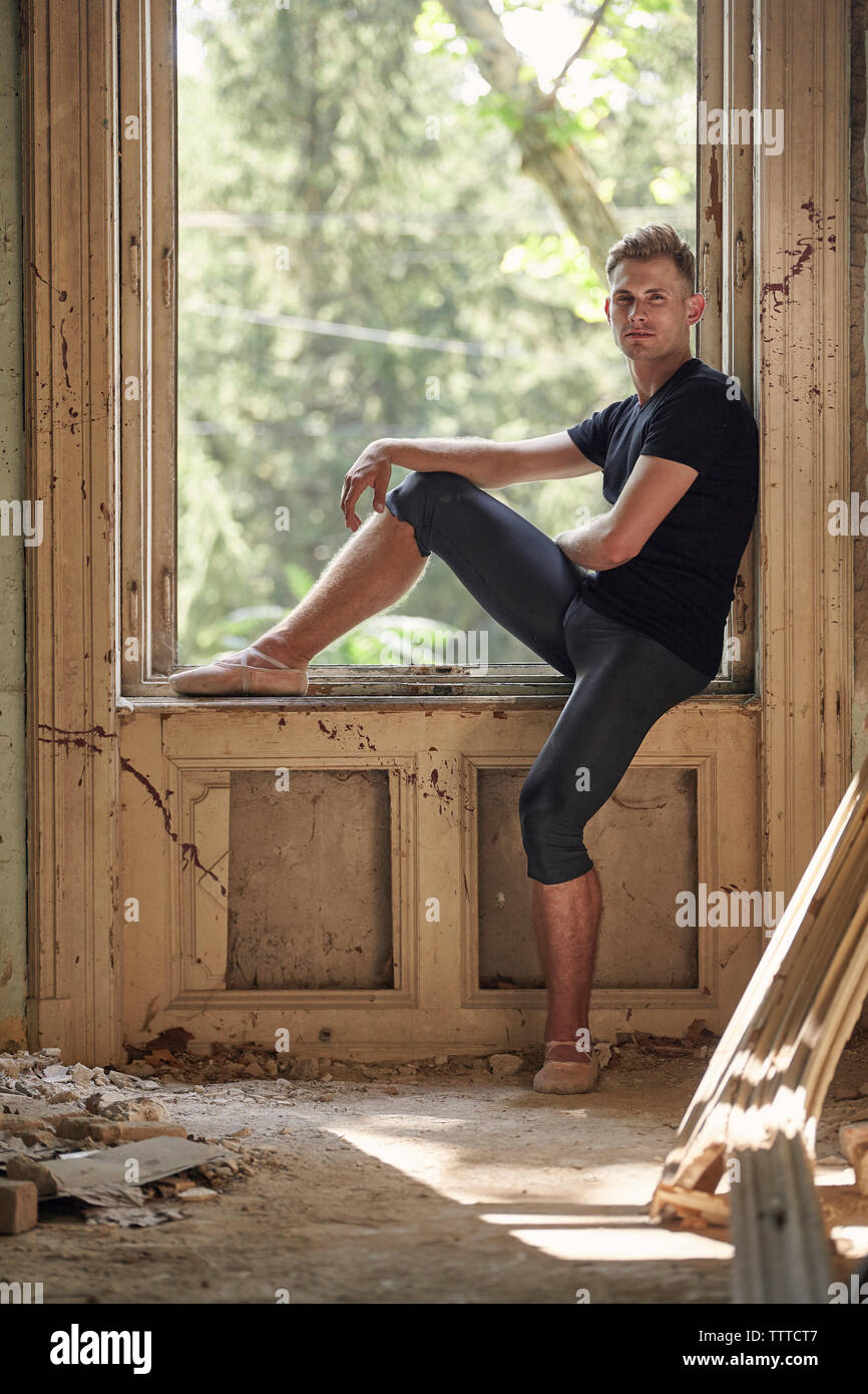 Side view of male ballet dancer sitting on window sill in old building ...