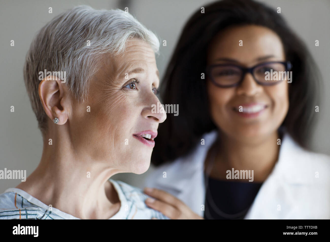 Happy female patient looking away with doctor in background Stock Photo ...