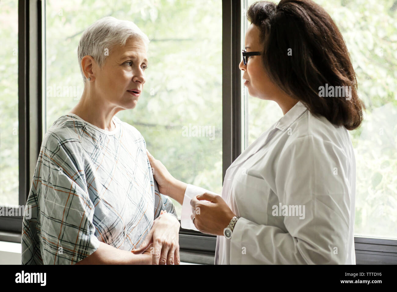 Doctor having discussion with patient while standing by window in ...