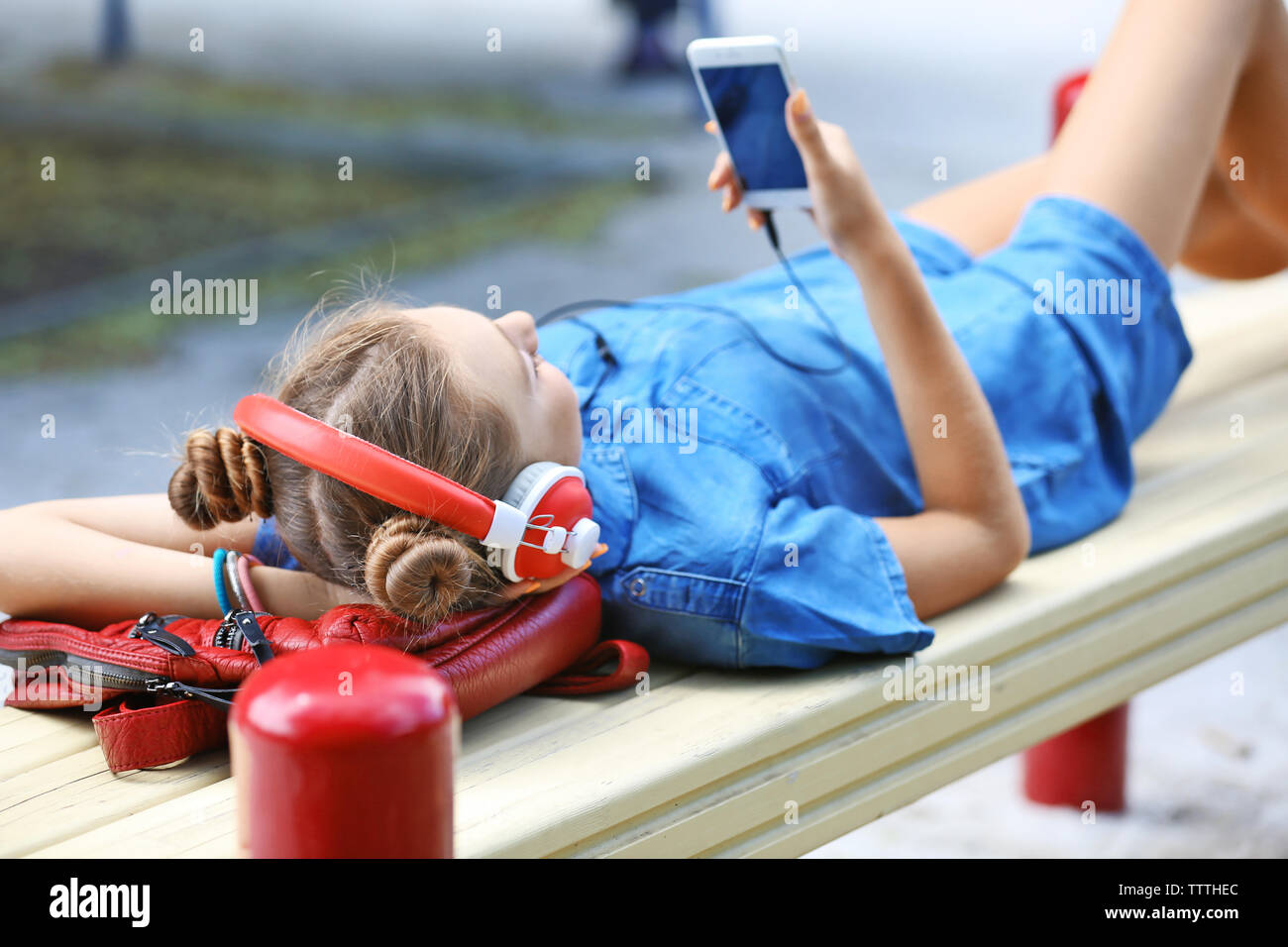 Cute young girl lying on bench in playground and listening music Stock ...