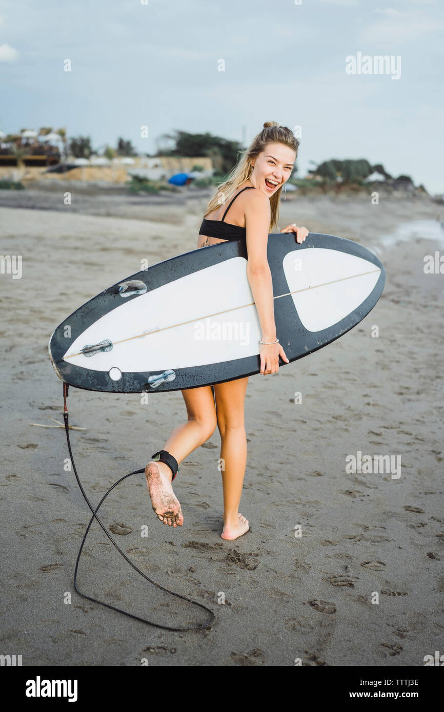 Cheerful woman carrying surfboard while walking at beach Stock Photo - Alamy