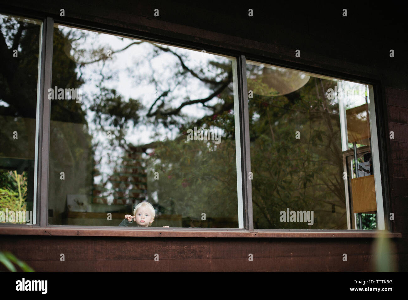 Curious boy looking through window from home Stock Photo - Alamy
