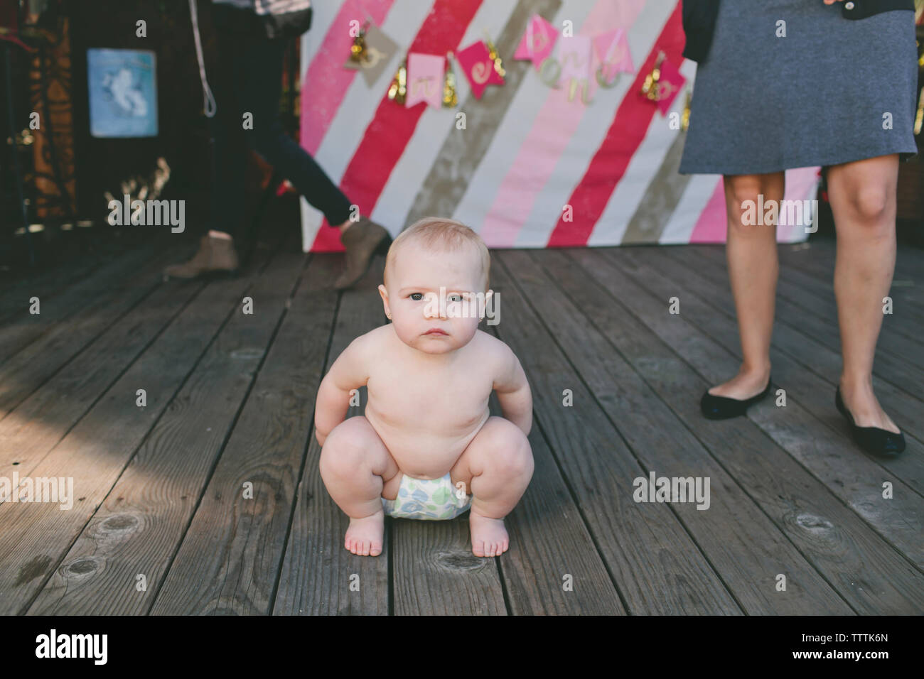 Portrait of shirtless baby girl crouching on floorboard at birthday ...