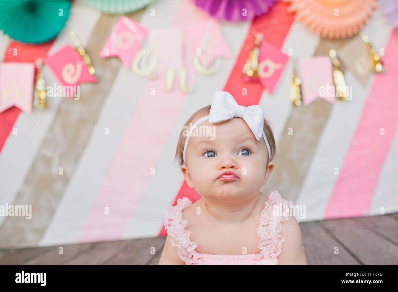 Cute baby girl puckering against decoration at her first birthday party ...