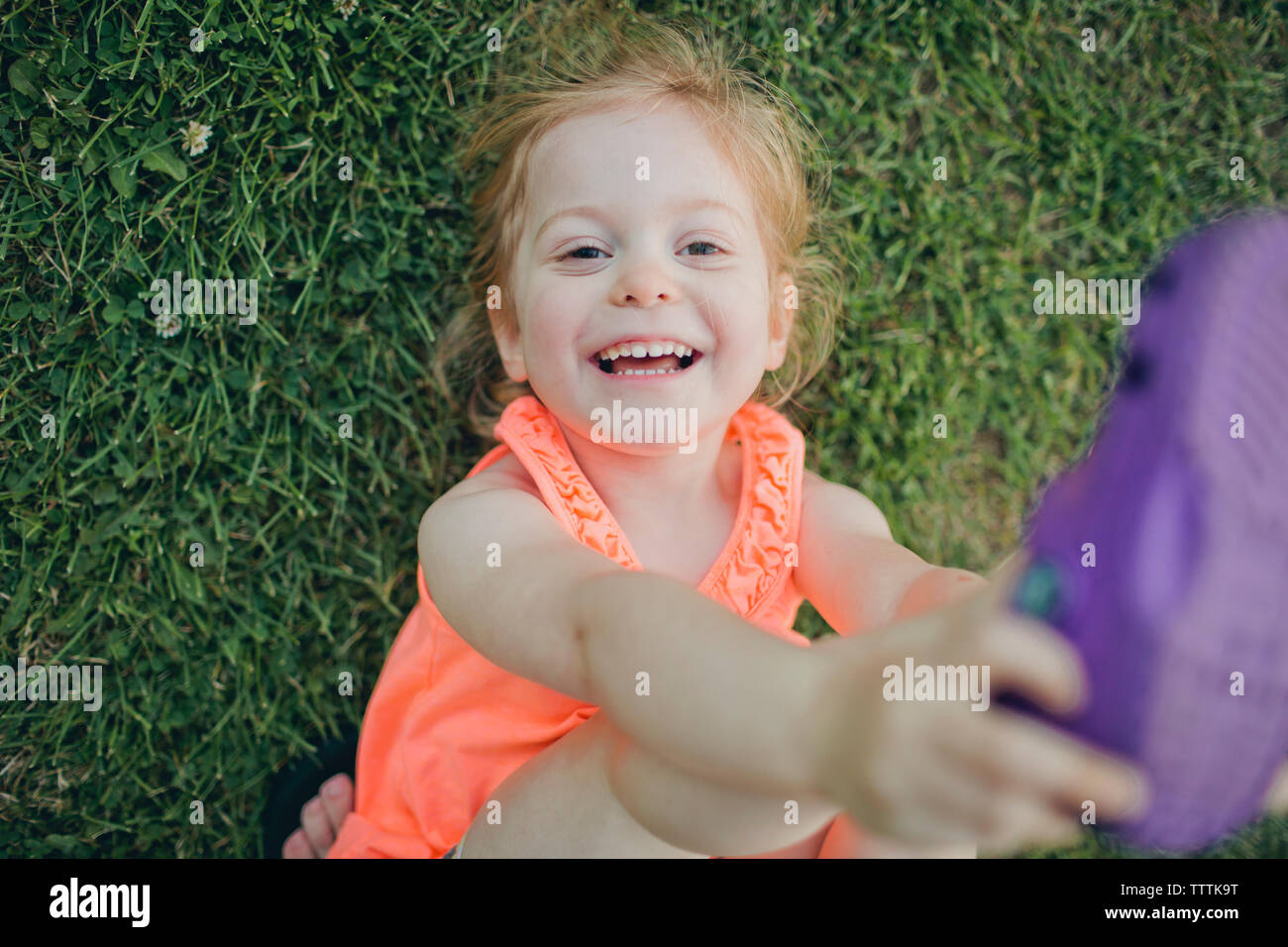 High angle portrait of cute happy girl lying on grassy field in park ...