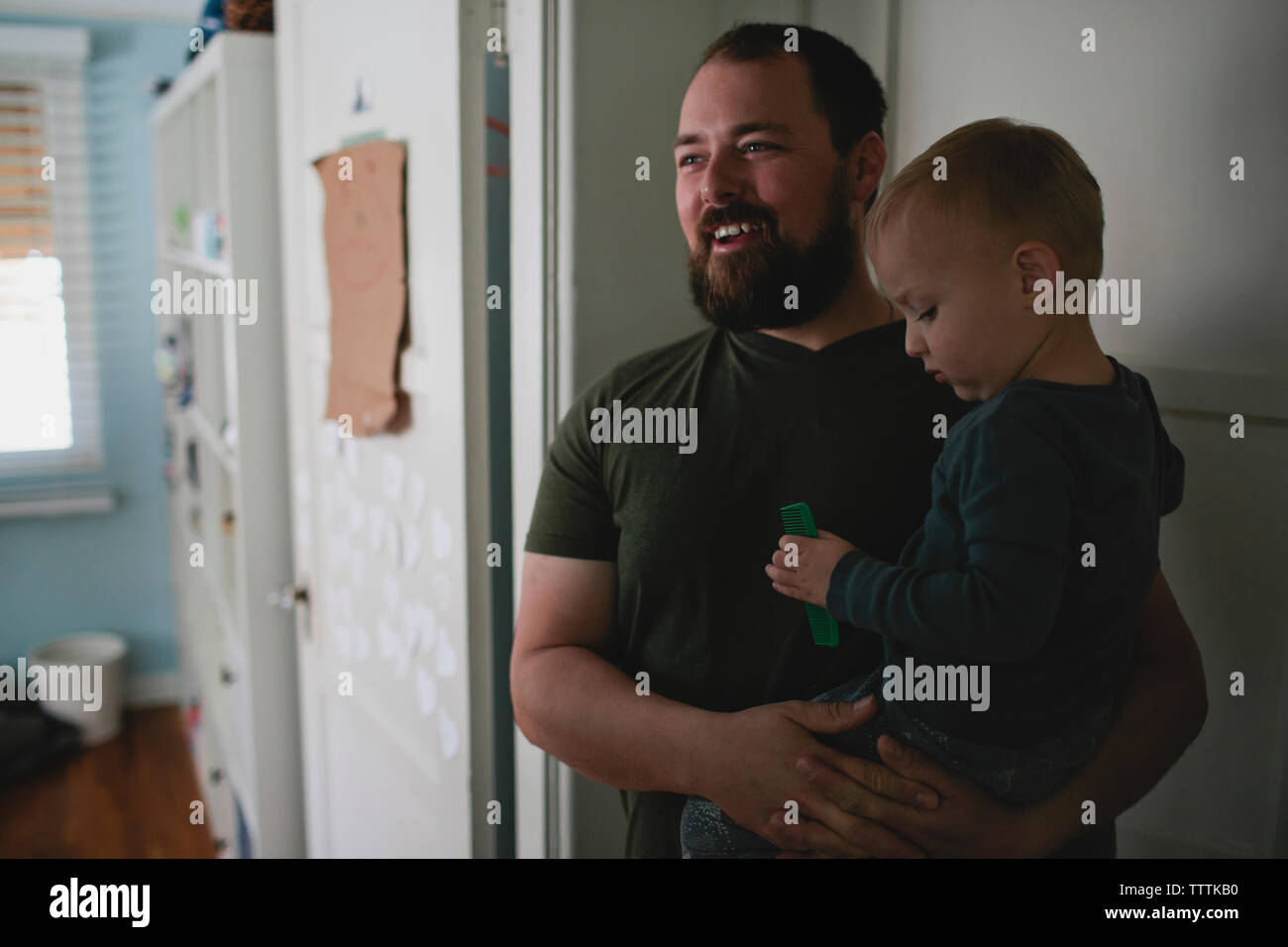 Smiling father looking away while carrying son at home Stock Photo - Alamy