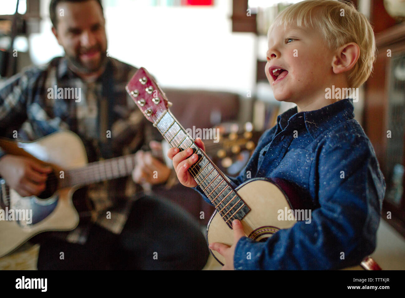 Father looking at son singing while playing guitar at home Stock Photo ...
