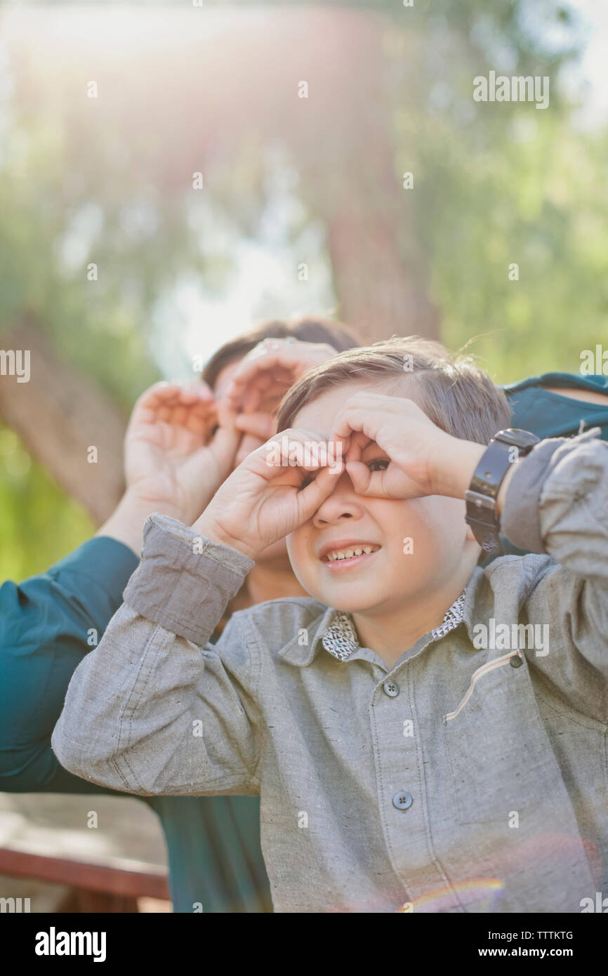Low angle view of playful father and son with hands around eyes looking ...