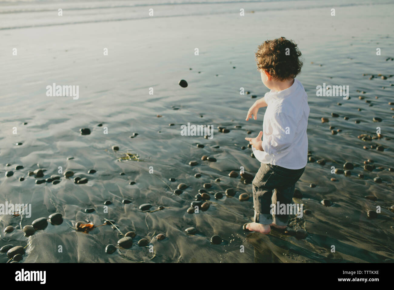 High angle view of playful boy throwing pebble while standing on shore ...