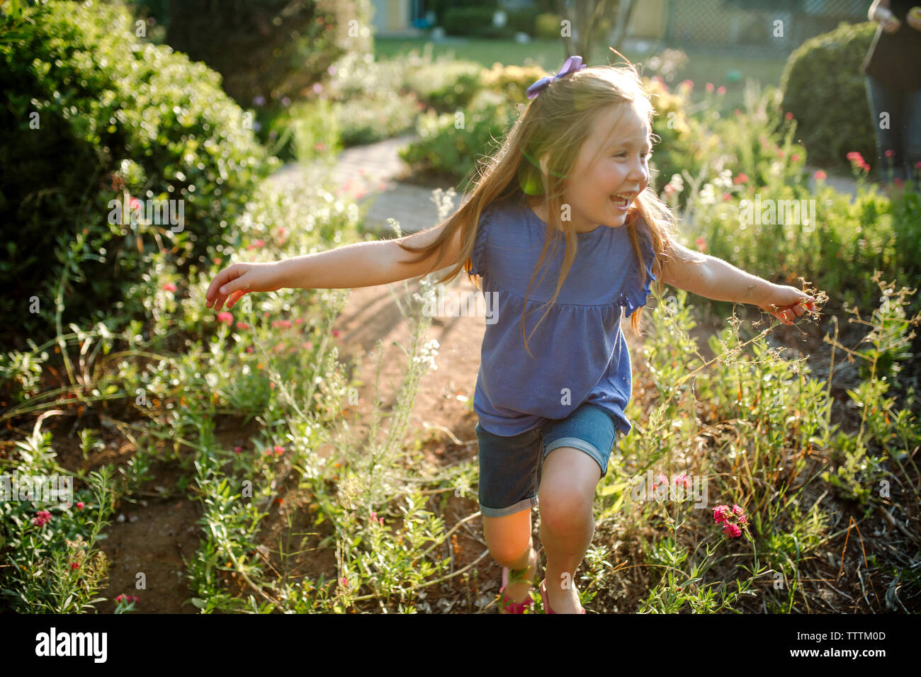 Carefree happy girl with arms outstretched running amidst plants at ...