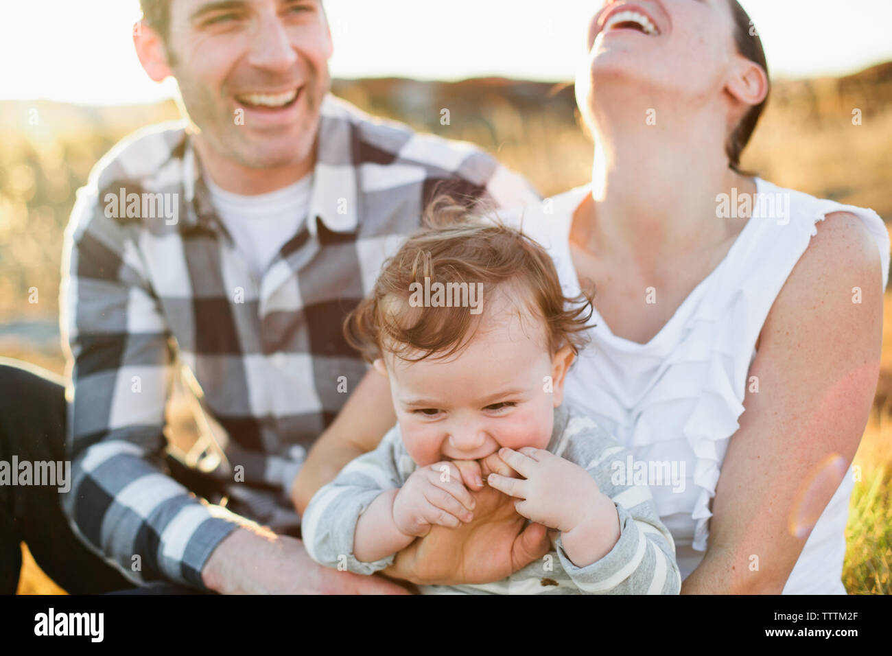 Playful son biting mother's hand while sitting by father at field Stock ...