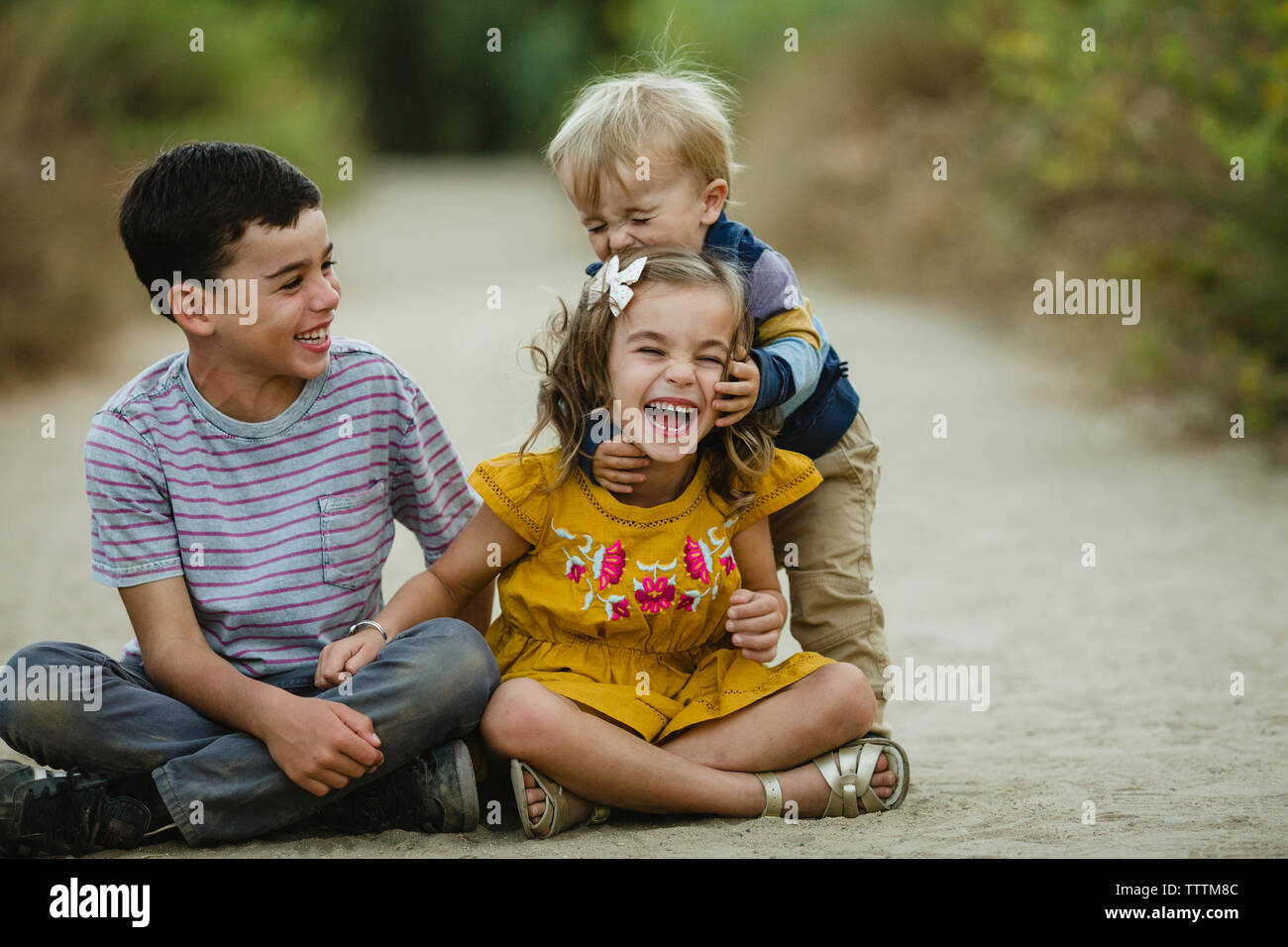 Cheerful boy looking at brother playing with sister on dirt road Stock ...