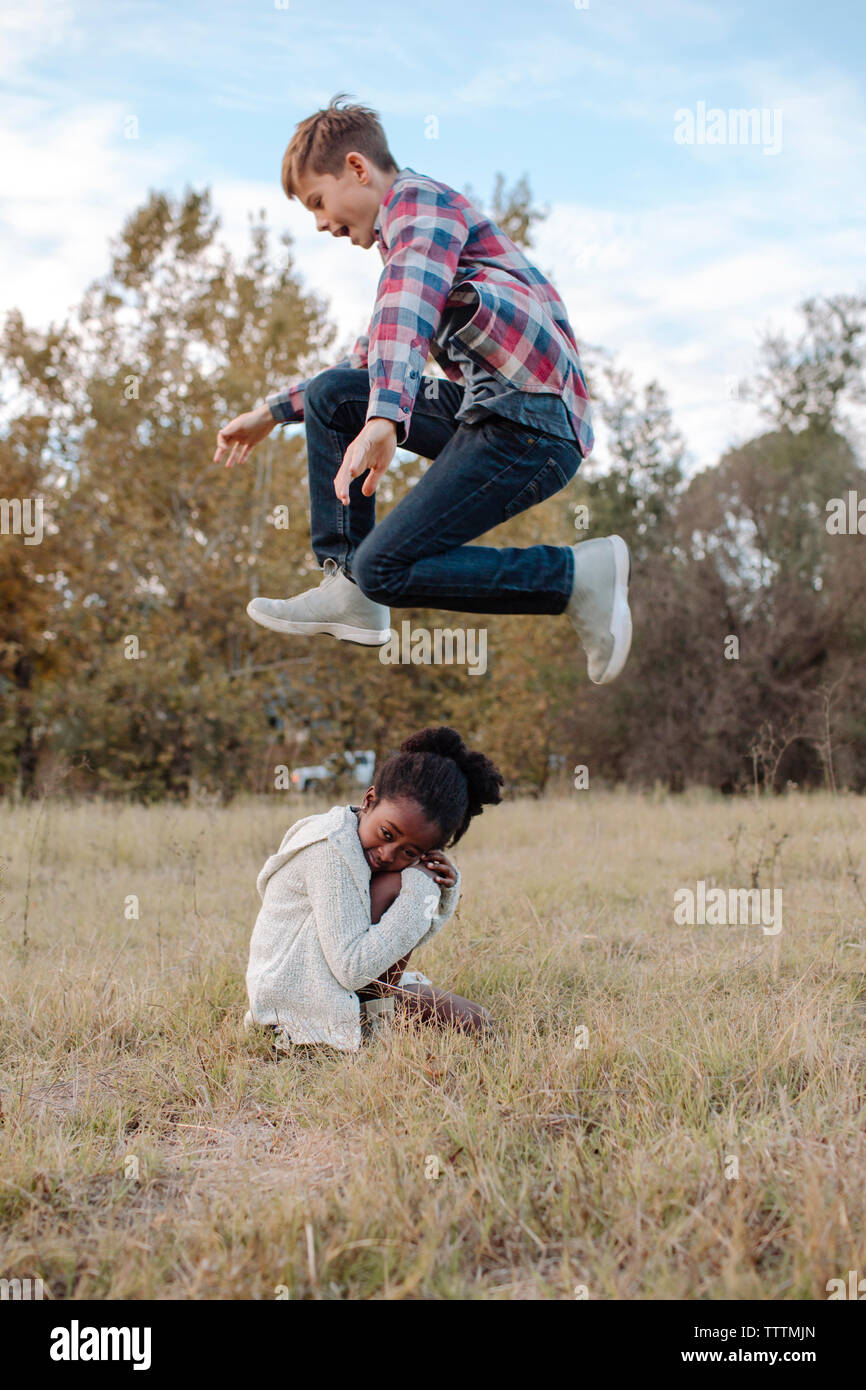 Side view of boy jumping over girl crouching on field at park Stock ...