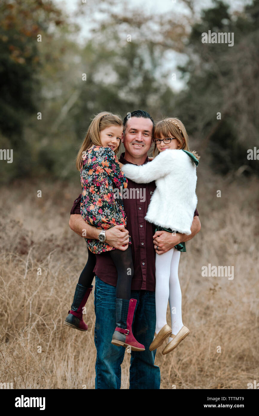 Portrait of happy father carrying daughters while standing on grassy ...