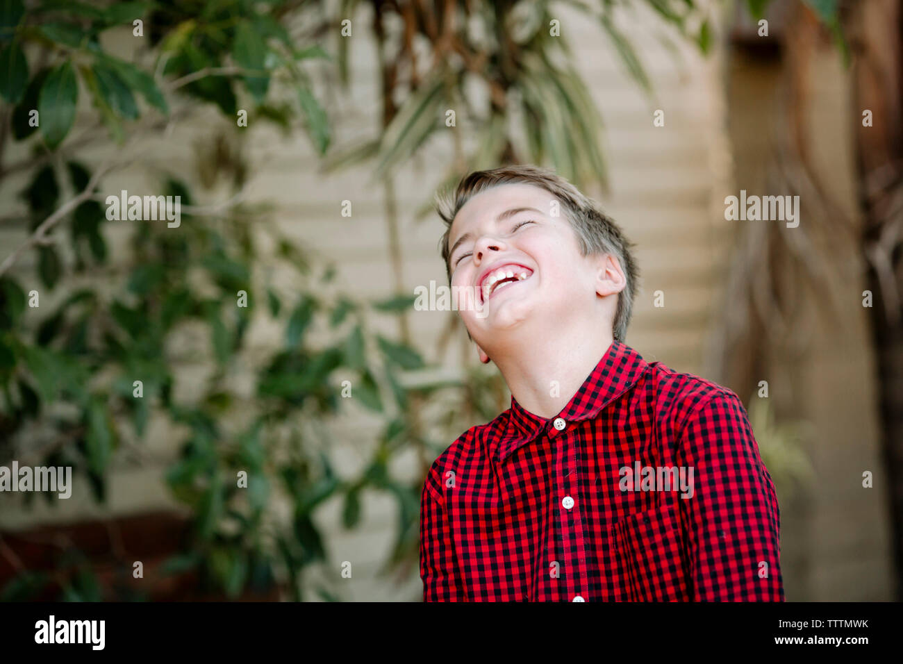 Close-up of happy boy laughing while standing against wall at yard ...