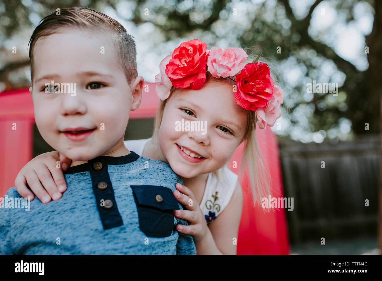 Portrait of cute smiling siblings standing against red garage in yard ...