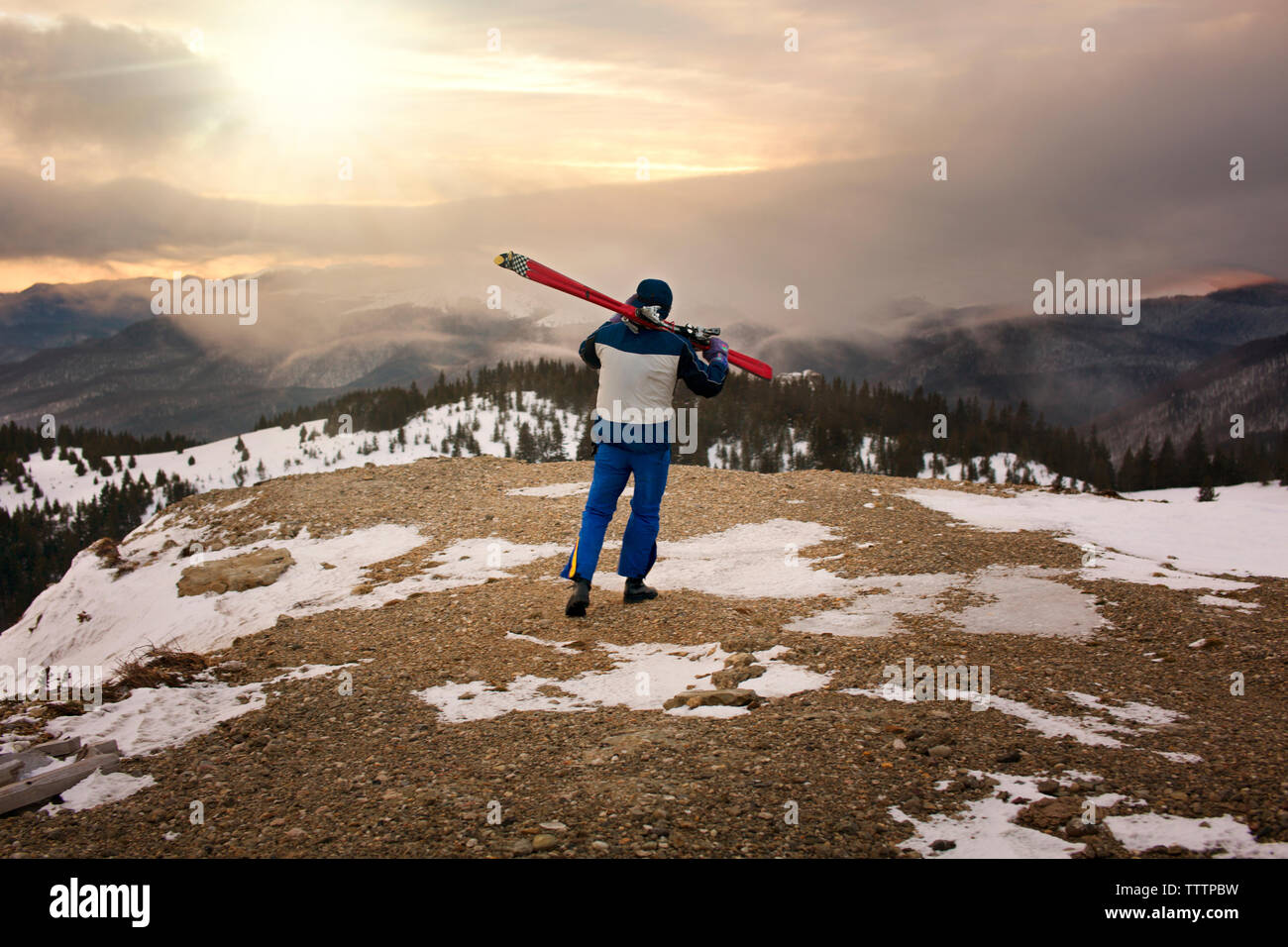 Rear view of man carrying ski while walking on mountain Stock Photo - Alamy
